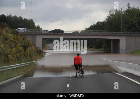 A bike rider comes to a halt as flood water blocks a road on the A555 ...