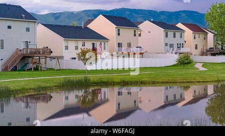 Shiny pond and pathway amid a grassy terrain in front of homes with ...