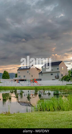 Vertical Pond surrounded by green grasses with homes and mountain ...