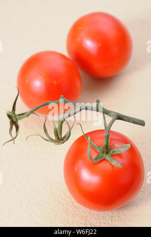 three vine tomatoes, on wooden board, placed in front of a black ...