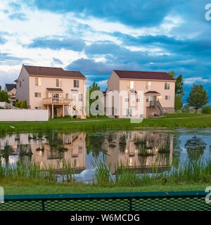 Green metal bench facing a shiny pond with reflection of homes and ...