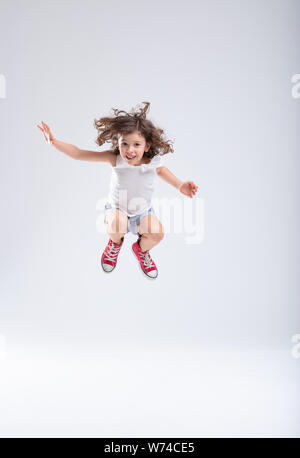 Hyperactive little girl leaping into the air with arms outstretched and ...