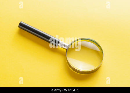 Magnifying glass lying diagonally on yellow with copy space viewed from ...