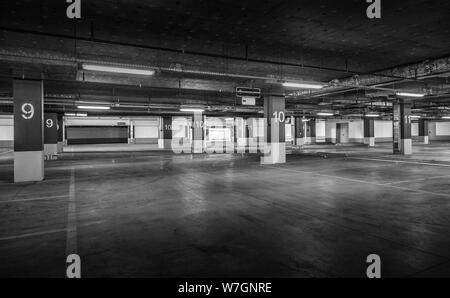 Grungy, dimly lit empty parking garage with overhead lights and an exit ...