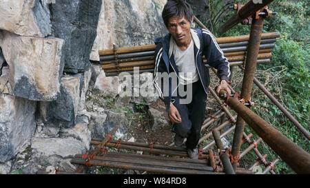 A Chinese villager carrying steel pipes climbs up a steel ladder on the ...