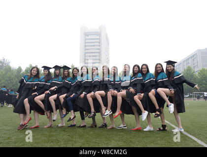 Chinese graduates dressed in academic gowns throw hats into the air to ...