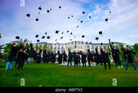 Chinese graduates dressed in academic gowns throw hats into the air to ...