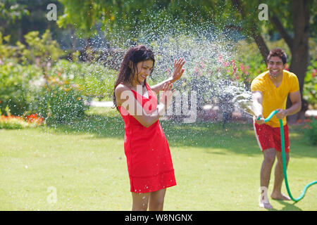 Boyfriend spraying water on his girlfriend with a hose in a garden ...