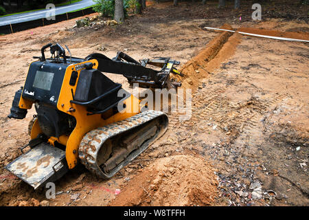A commercial ditch digging machine cutting a trench in yard to install ...