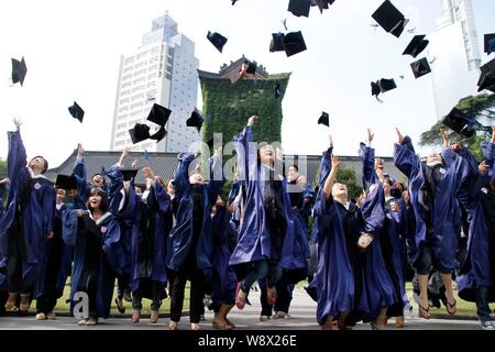 Chinese graduates dressed in academic gowns throw hats into the air to ...