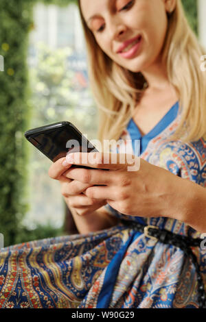 Smiling young adult woman checking her cell phone and holding a ...