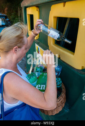 Hand dropping glass bottles into a green miniature bin, representing ...