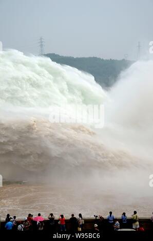 Visitors look at water gushing out from the Xiaolangdi Dam at the ...
