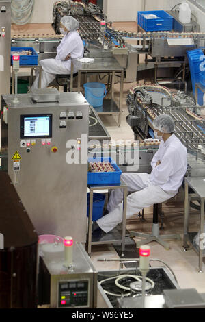 Factory workers watch bottles of Yakult fermented milk drink passing ...
