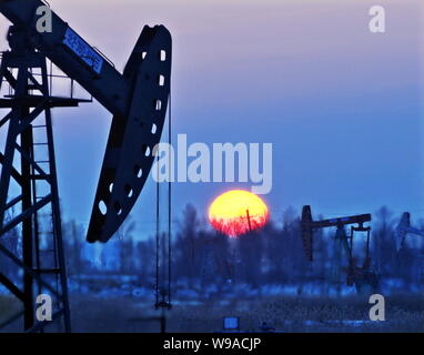 --FILE--Oil derricks pump crude oil at sunrise at an oil field in ...