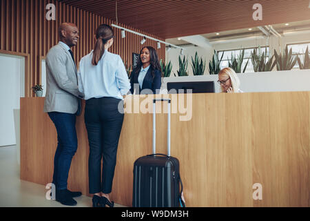 Two smiling guests talking to a concierge while checking in together at ...