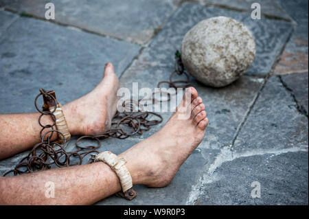 Prisioner with ball and chain in the court of the prison. Close up ...