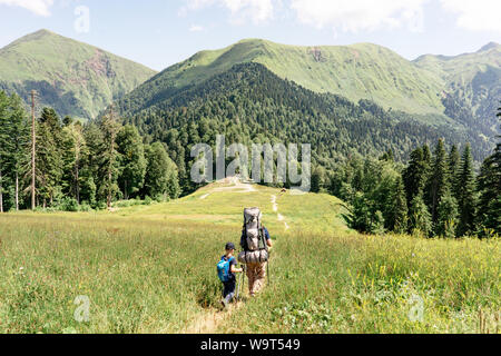 Dad and son child with tourist backpacks at low wooden fence on green ...