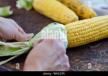 The woman is peeling corn shells on dark wooden table Stock Photo - Alamy