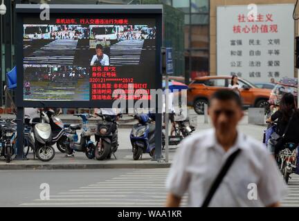 Pedestrians walk across a crossroad as a big electronic screen ...