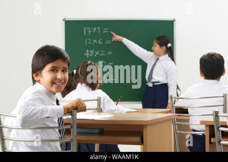 Schoolboy looking back towards camera and schoolgirl teaching her ...