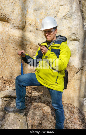 male geologist in helmet and protective glasses examines a sample of ...