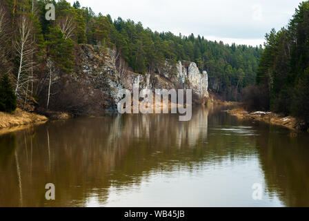 river bank with limestone cliffs overgrown with pine forest in early ...