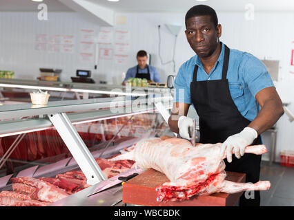 African American male butcher processing carcase of young lamb for sale ...