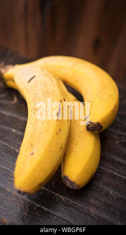 Ripe Cavendish bananas with small bruises positioned on a wooden brown ...