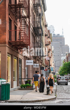A group of people walking along a city street in front of a row of ...