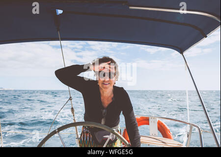 Mature woman standing on boat, laughing, wind blowing dress Stock Photo ...