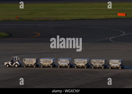 A small car towing baggage containers for loading onto an airliner on ...