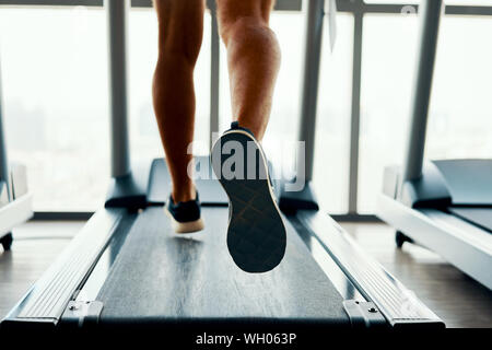 Close up male muscular feet in sneakers running on the treadmill at gym ...