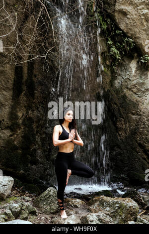 Woman practising yoga at waterfall, tree position Stock Photo - Alamy