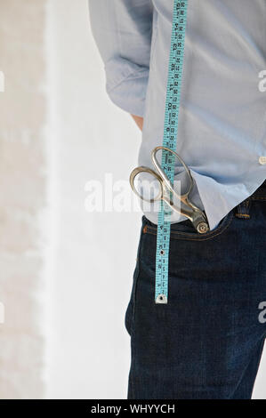 Tailor with scissors in pocket and measuring tape, standing indoors ...