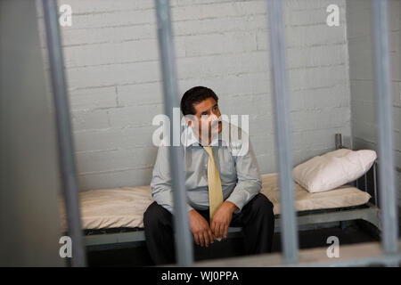 Criminal sitting on bed in jail Stock Photo - Alamy
