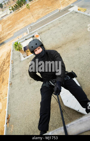 High angle view of a armed man rappelling down the rope from building ...
