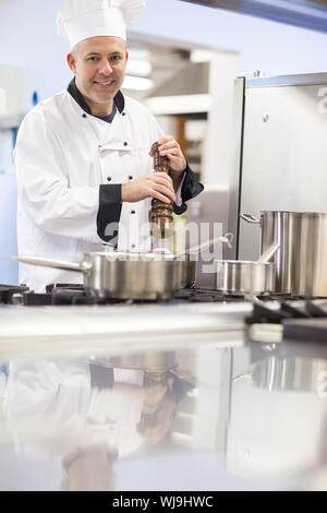 Smiling head chef flavoring food with pepper in professional kitchen ...