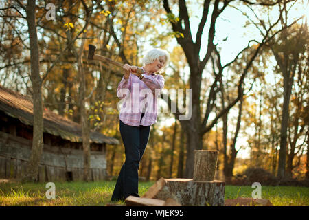 A middle-aged woman is chopping wood under a shed Stock Photo - Alamy