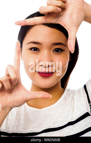 A smiling asian woman framing her face with her hands against a white ...