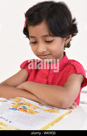 Female child reading open book while standing by library bookshelf with ...