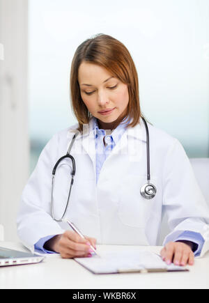 Asian healthcare worker taking notes while working on laptop computer ...