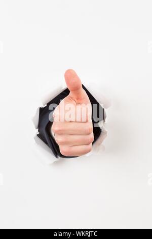 Thumbs up bursting through paper on white background Stock Photo - Alamy