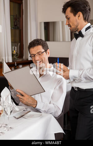 Waiter serving a young couple seated at a table holding menus in a ...