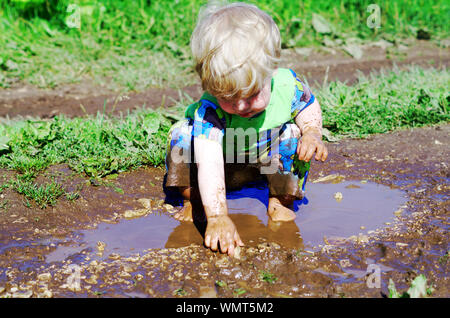 boys playing in the mud while baby brother in a diaper watches from the ...