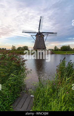 Dutch windmill laying along the canal with wild grass blown by strong ...