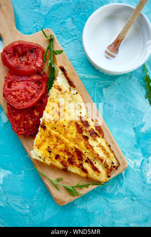 Grilled pike fillet with tomatoes on wooden board on blue background ...