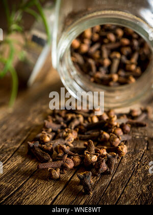 Glass jar and spoon with aromatic cloves on wooden table. Space for ...