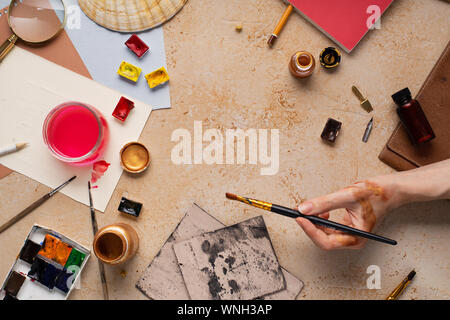 Artist's workspace flatlay with female hands holding a brush. Art ...