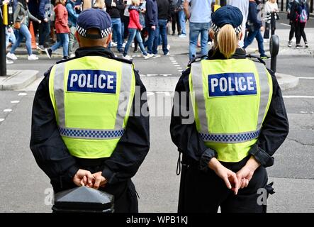 BACK VIEW OF TWO POLICE OFFICERS, MALE AND FEMALE, WALKING DOWN THE ...